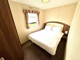 Quarto de hotel com uma cama de solteiro, janela com cortinas, cabeceira e uma pequena mesa de cabeceira com abajur.