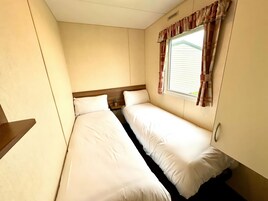 Acomodação pequena, um quarto com duas camas, janela com cortinas e cabeceira de madeira.