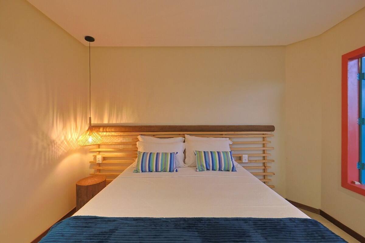 Quarto com cama, abajur e janela com moldura vermelha.
