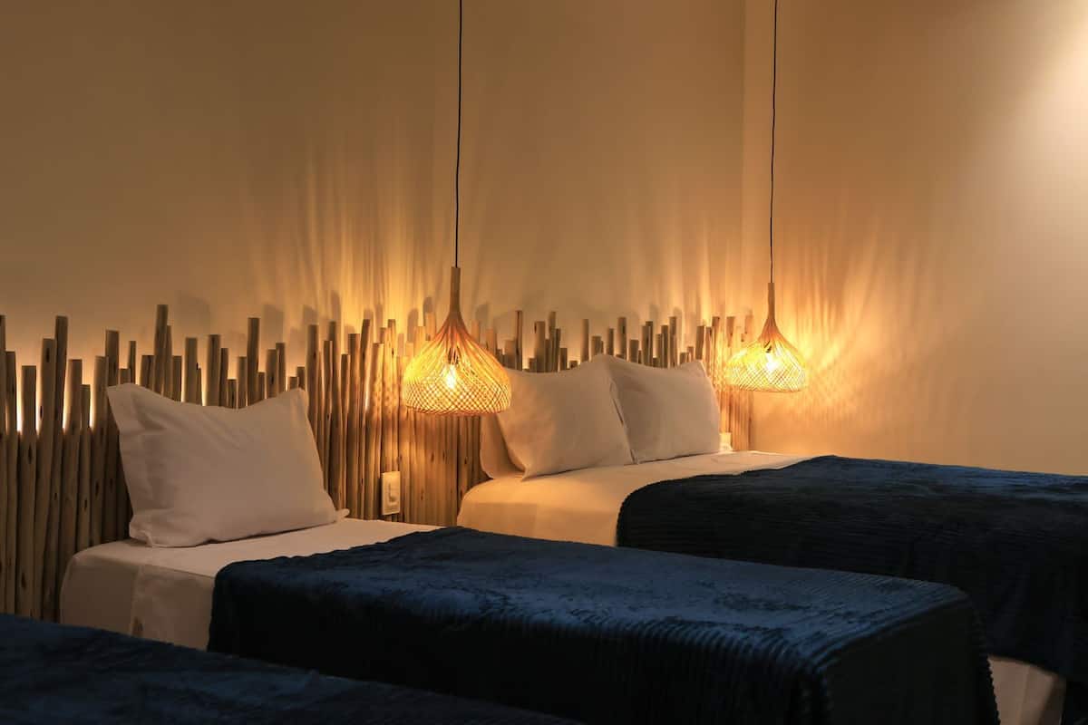 Quarto de hotel moderno com painel de parede em madeira, duas camas com roupa de cama branca e luminárias pendentes.