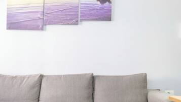 Uma sala de estar com um sofá cinzento, uma mesa de centro e um tríptico de pintura pendurado na parede.