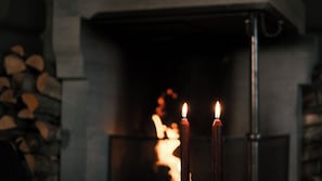 Duas velas em frente a lareira com lenha à mostra.