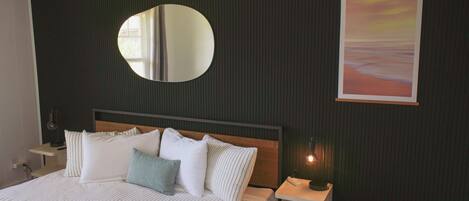 Cama bem arrumada com roupa de cama listrada, um espelho redondo, uma mesa de cabeceira com abajur e um quadro na parede.