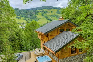 Uma cabana de madeira com hidromassagem e área de estar externa, rodeada por vegetação exuberante e vista para colinas ondulantes.