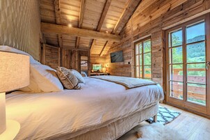 Quarto acolhedor de cabana de madeira com uma cama grande, televisão e janela com vista para uma área arborizada.