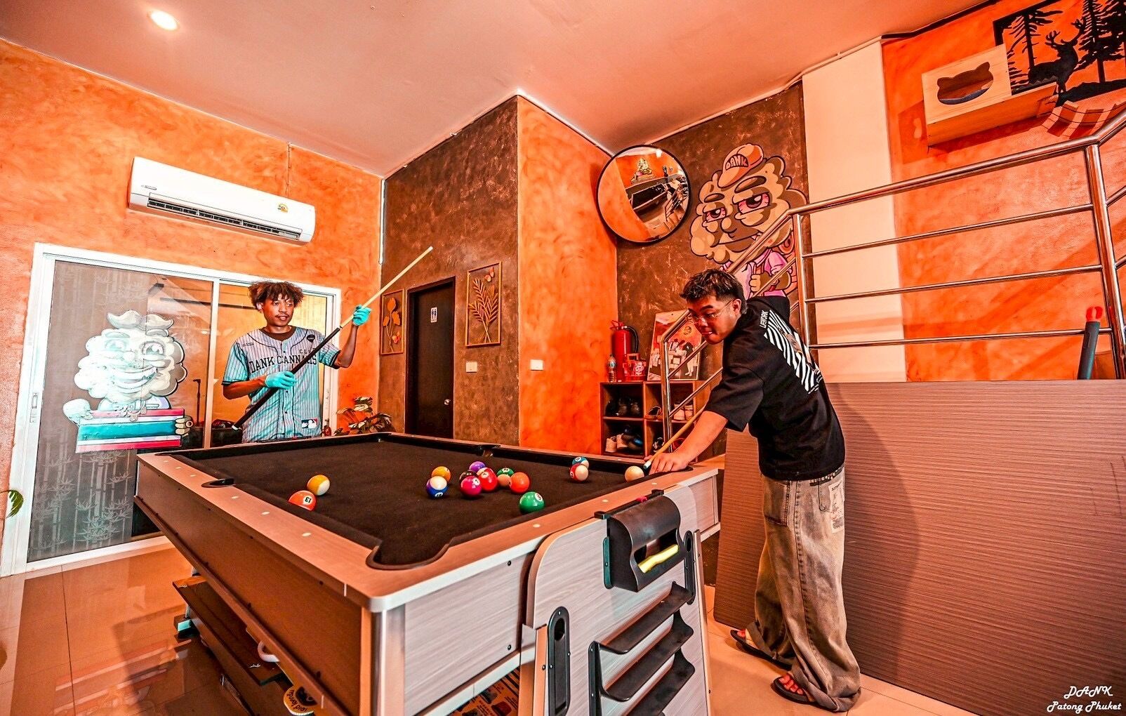 Uma mesa de bilhar em um quarto com paredes laranja, um espelho e uma decoração com personagem de desenho animado.