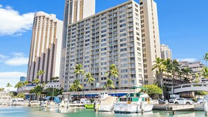 Um hotel à beira-mar com vários edifícios altos, um porto com barcos e palmeiras.
