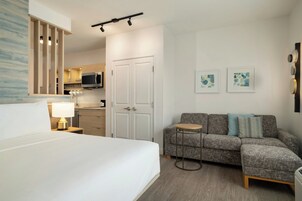 Quarto de hotel com cama, sofá, mesa pequena, micro-ondas, armário e porta.