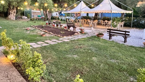 Uma área de jardim com espaço de refeições, incluindo mesas e cadeiras sob uma tenda.