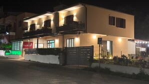Um edifício de dois andares com teto plano, entrada protegida por grades e placa indicando um restaurante chamado "FlameGo Pizza Cuisine".