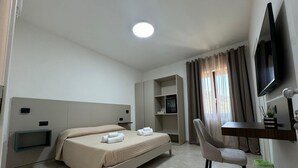 Quarto de hotel com duas camas, uma escrivaninha, uma cadeira, televisão e uma janela com cortinas.