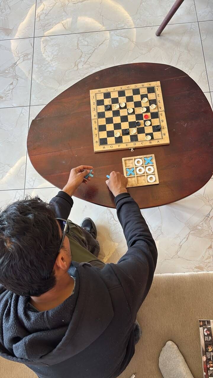 Uma pessoa jogando xadrez em uma mesa redonda de madeira com um tabuleiro quadriculado.