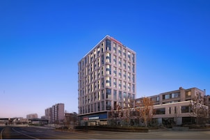 Um hotel de vários andares com design moderno, apresentando uma entrada marcante e uma vista clara da área urbana circundante.