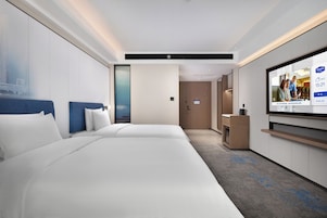 Quarto de hotel com duas camas, televisão, escrivaninha e vista para a paisagem urbana.