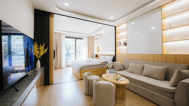 Quarto de hotel moderno com cama, sofá, televisão e uma pequena mesa com um vaso de flores.
