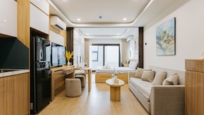 Quarto de hotel moderno com cozinha compacta, sofá, mesa de centro e uma janela grande.