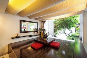 Um interior moderno com soalho de madeira escura, uma mesa central com um vaso de flores e um espelho grande na parede.
