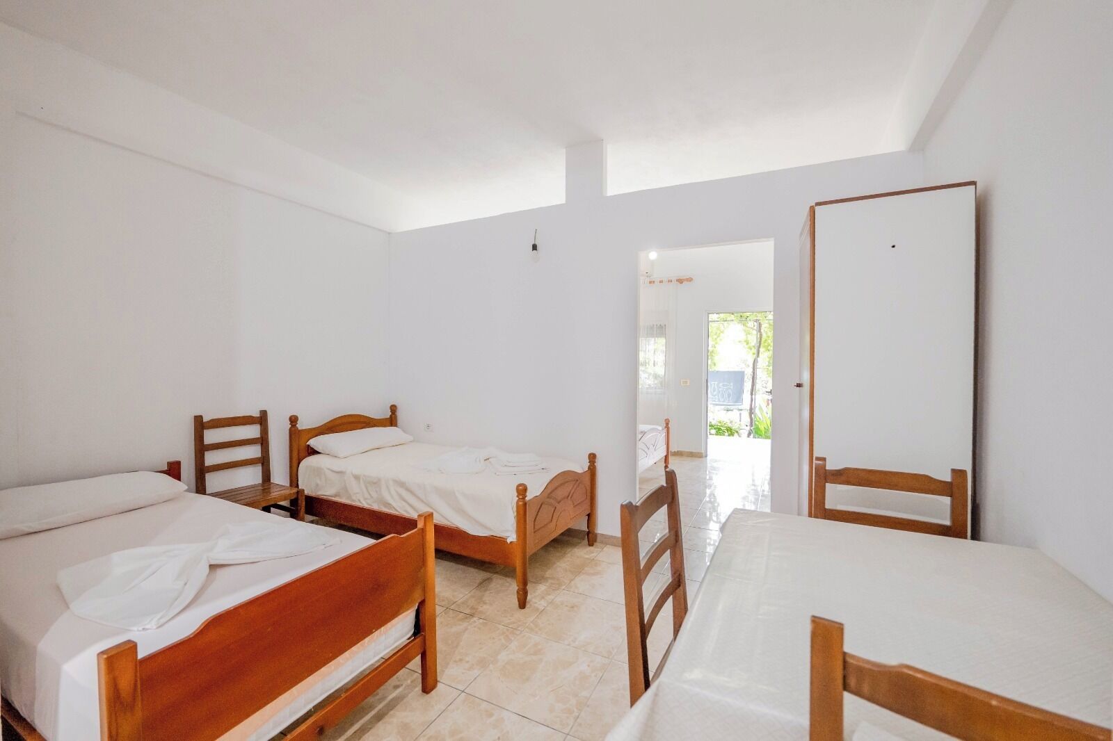 Quarto com três camas de madeira, um espelho grande e uma porta que dá para uma varanda.