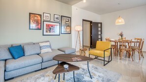 Uma sala de estar moderna com um sofá cinzento, uma poltrona amarela, uma mesa de jantar de madeira e um abajur.