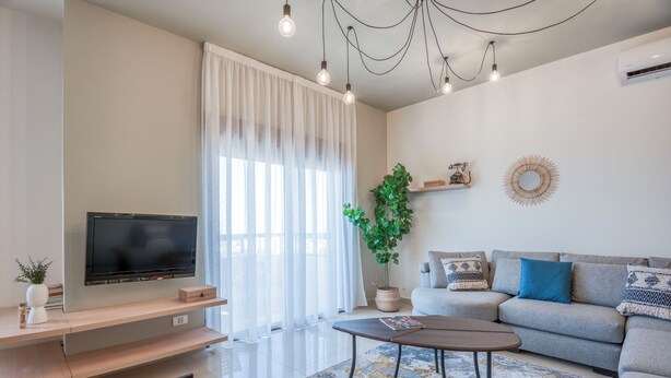 Uma sala de estar moderna com televisão de tela plana, sofá, mesa de centro e um vaso de planta.