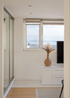 Quarto moderno com uma janela grande, um armário branco e um vaso sobre o armário.
