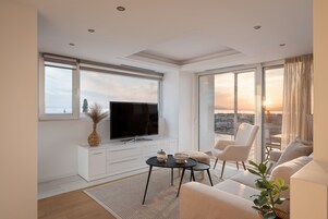 Sala de estar moderna com televisão de tela plana, móveis brancos, uma grande janela com vista para a cidade e uma varanda com vista.