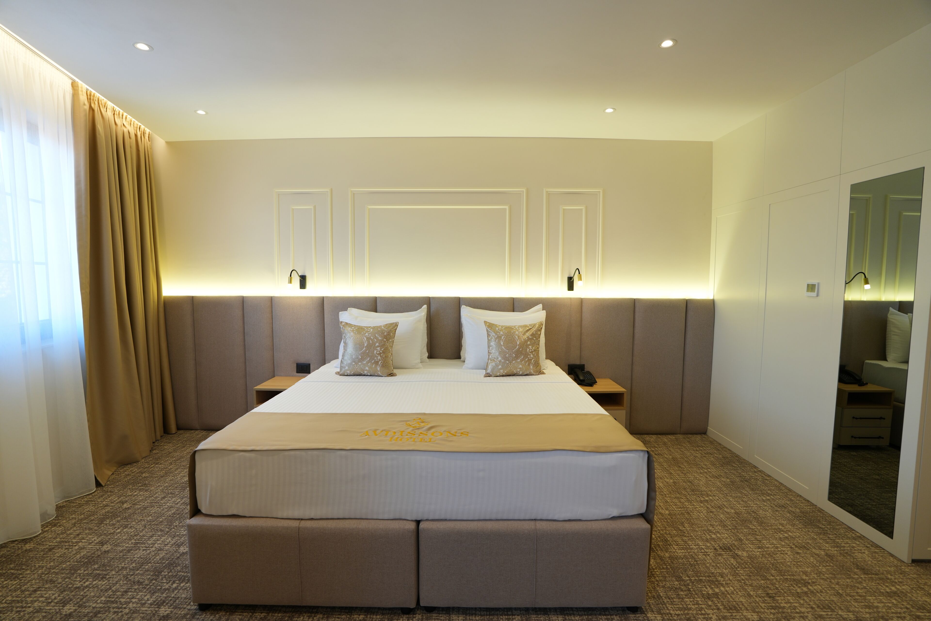 Quarto de hotel com uma cama grande, mesas de cabeceira, um guarda-roupa e um espelho.