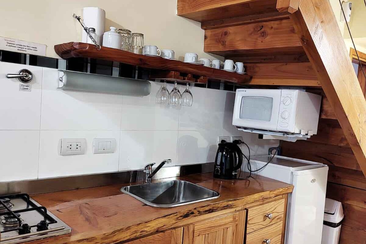 Uma cozinha compacta com fogão a gás, pia, micro-ondas e armários de madeira.