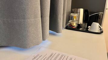 Quarto de hotel com uma cama, mesa de cabeceira com cafeteira, bandeja com xícara e pires e menu na mesa.