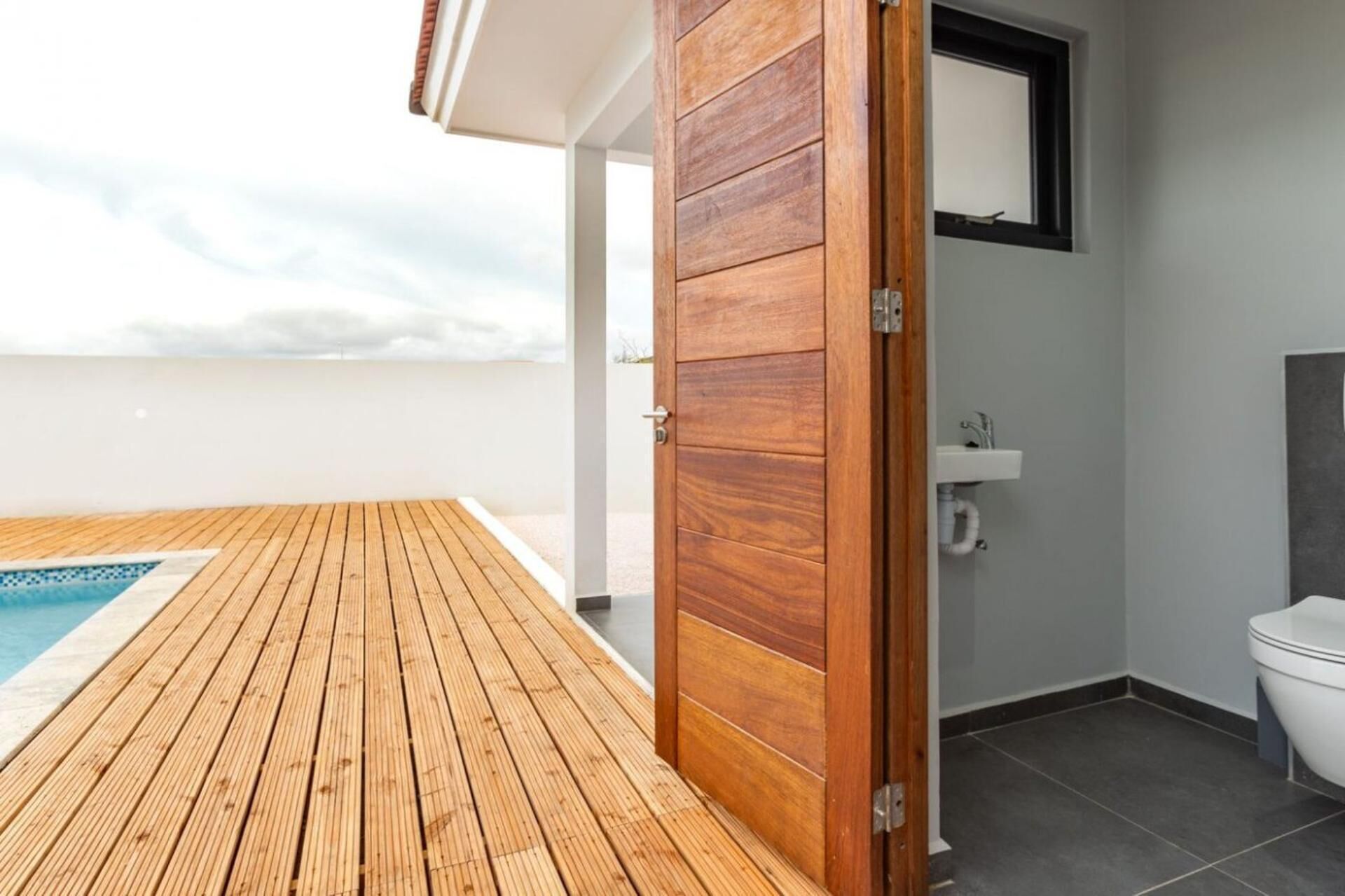 Um deck de madeira com piscina, um banheiro com pia e vaso sanitário, e uma porta de madeira grande.