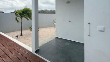Um espaço de estar moderno e amplo, com deck de madeira, uma pequena palmeira e vista do céu.