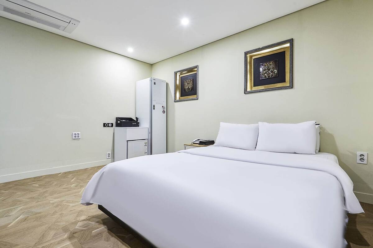 Quarto de hotel com uma cama grande, um guarda-roupa, uma escrivaninha com telefone e duas imagens emolduradas na parede.