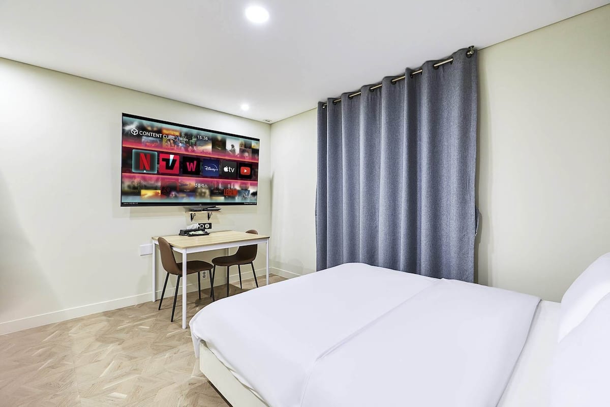 Quarto de hotel com cama, secretária com cadeira, televisão de tela plana na parede e janela com cortinas.