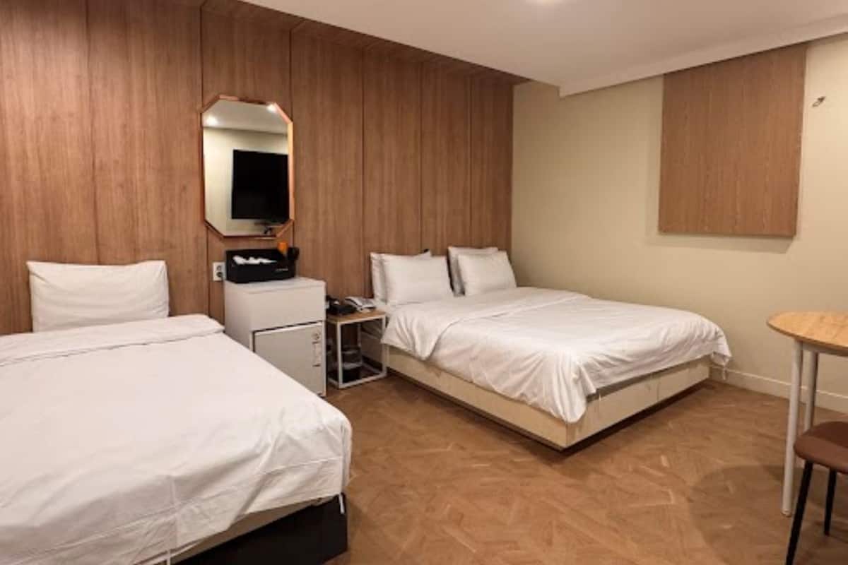Quarto de hotel com duas camas de solteiro, um guarda-roupa de madeira, uma pequena secretária com cadeira e uma televisão.