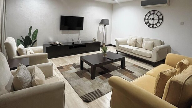 Uma sala de estar moderna com televisão de tela plana, mesa de centro, sofás e um relógio na parede.