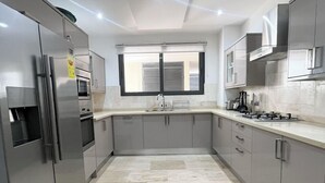 Uma cozinha moderna com eletrodomésticos de aço inoxidável, uma janela com persianas e piso ladrilhado.