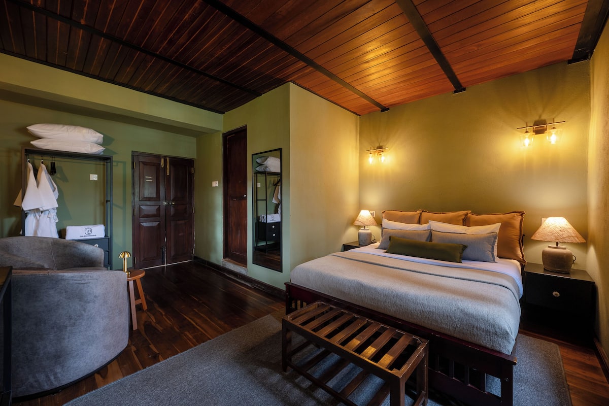 Quarto com cama grande, abajures, um banco de madeira, uma cadeira e um guarda-roupa.