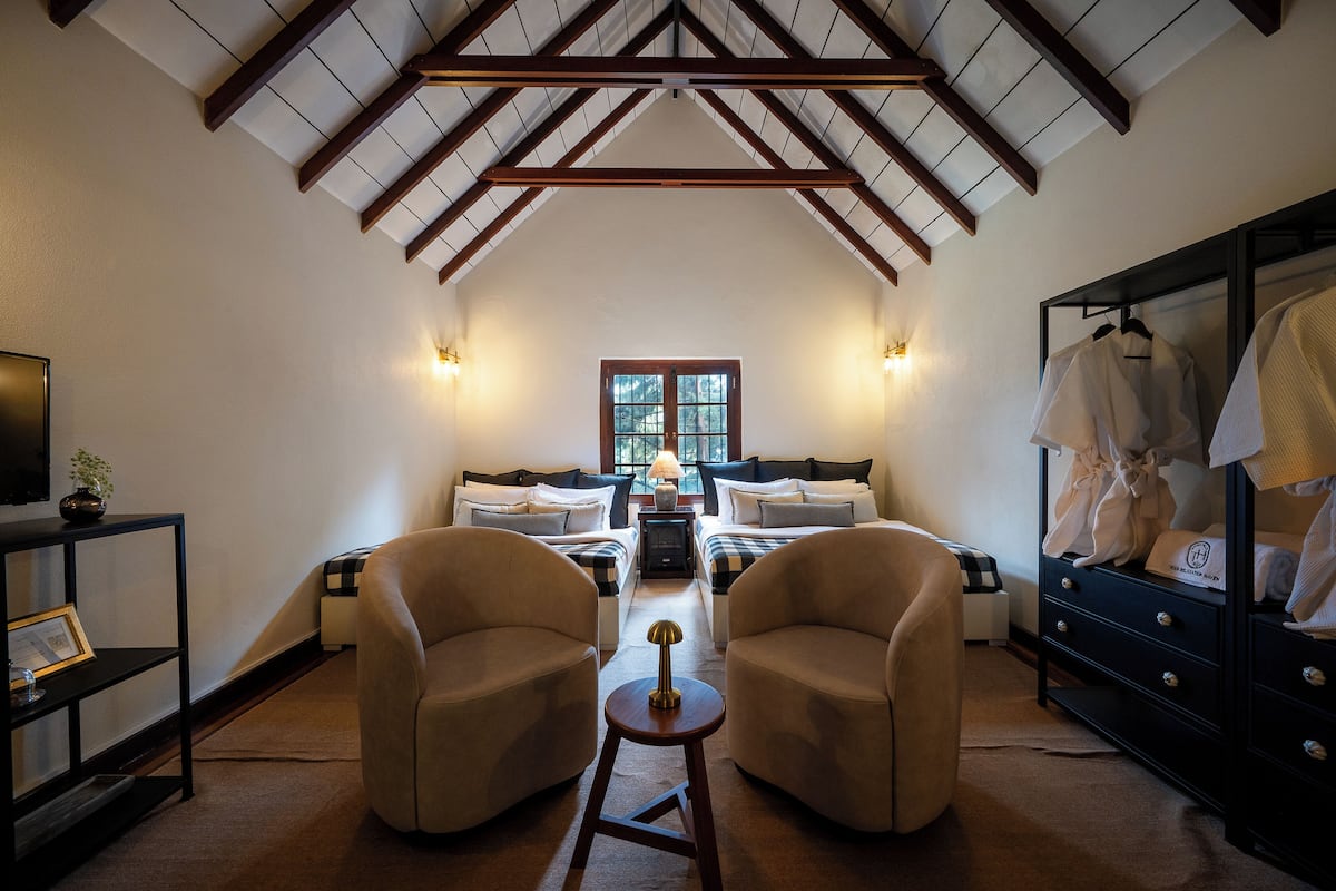 Quarto com teto abobadado, dois sofás, uma mesa pequena, cama com janela e cômoda com toalhas.
