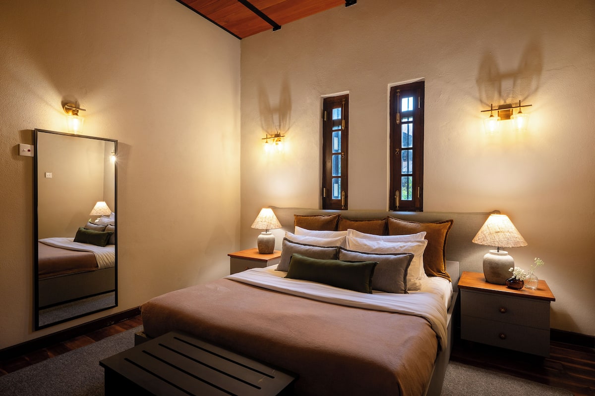 Quarto bem arrumado com cama, abajures, espelho e mesa de cabeceira.