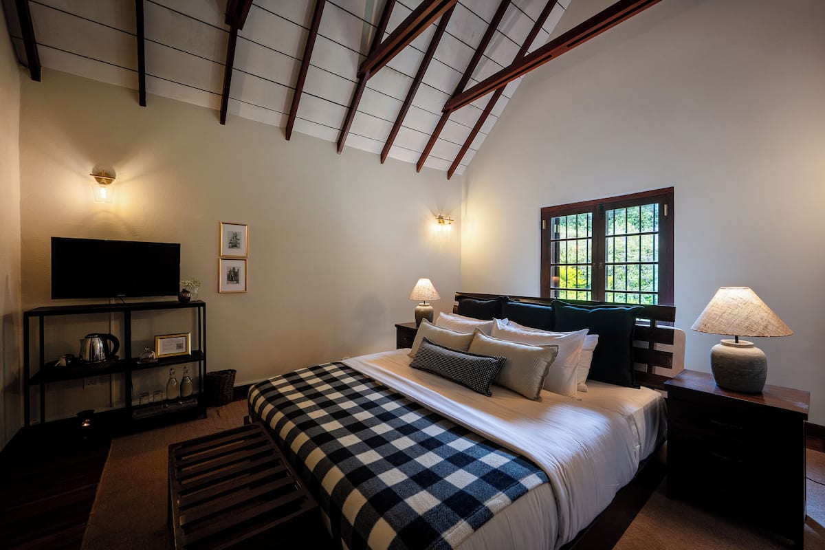 Quarto com cama grande, televisão, escrivaninha e janela com vista para o verde.