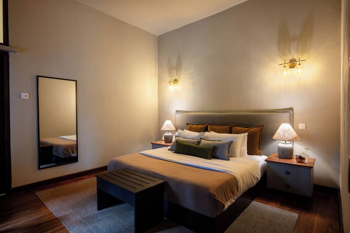 Quarto bem arrumado com uma cama grande, abajures, uma mesa de cabeceira, uma mesinha e um espelho na parede.