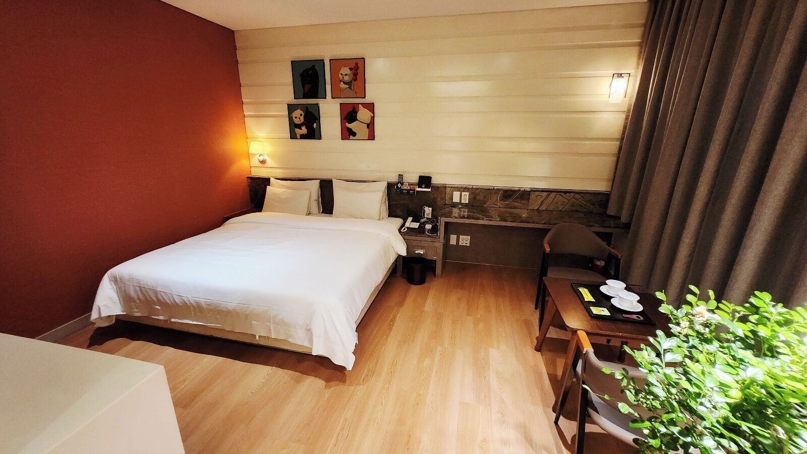 Quarto de hotel com cama, escrivaninha, cadeira e uma pequena mesa com xícaras.