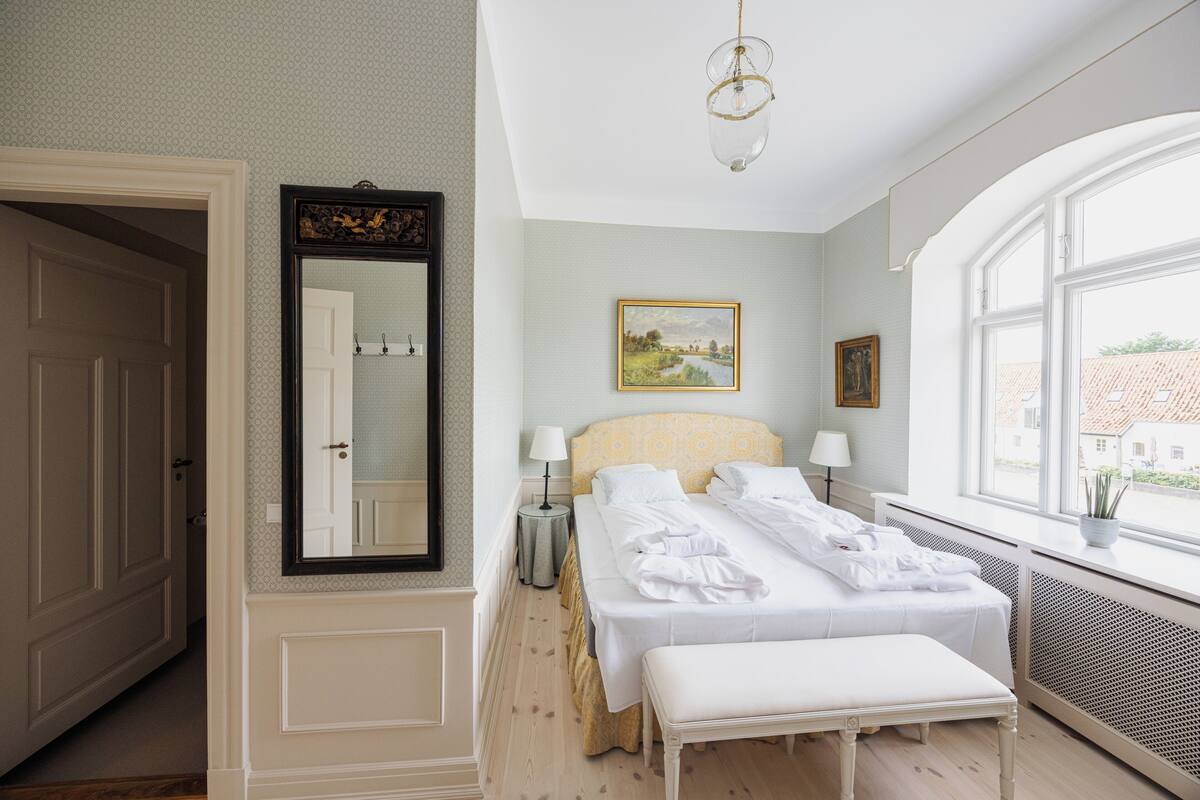 Quarto bem arrumado com uma cama grande, mesa de cabeceira, espelho e janela com vista.