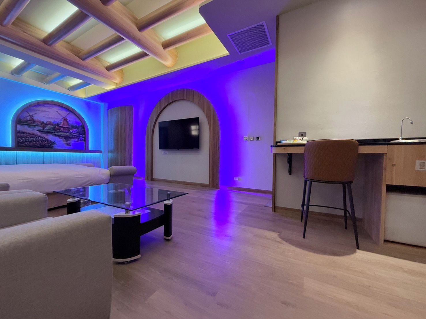 Quarto moderno com mesa de vidro, sofá, escrivaninha com cadeira e TV fixada na parede.