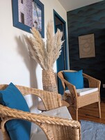 Quarto com móveis de vime, um vaso com plumas de capim-dos-pampas e um quadro na parede.
