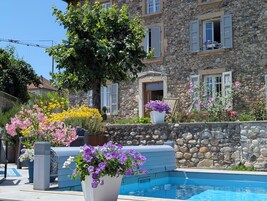 Um edifício de pedra com piscina, rodeado por diversas flores e plantas.