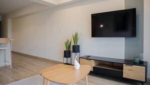 Uma sala de estar moderna com uma mesa de madeira, duas plantas em vasos, uma TV de tela plana e um rack de entretenimento preto.