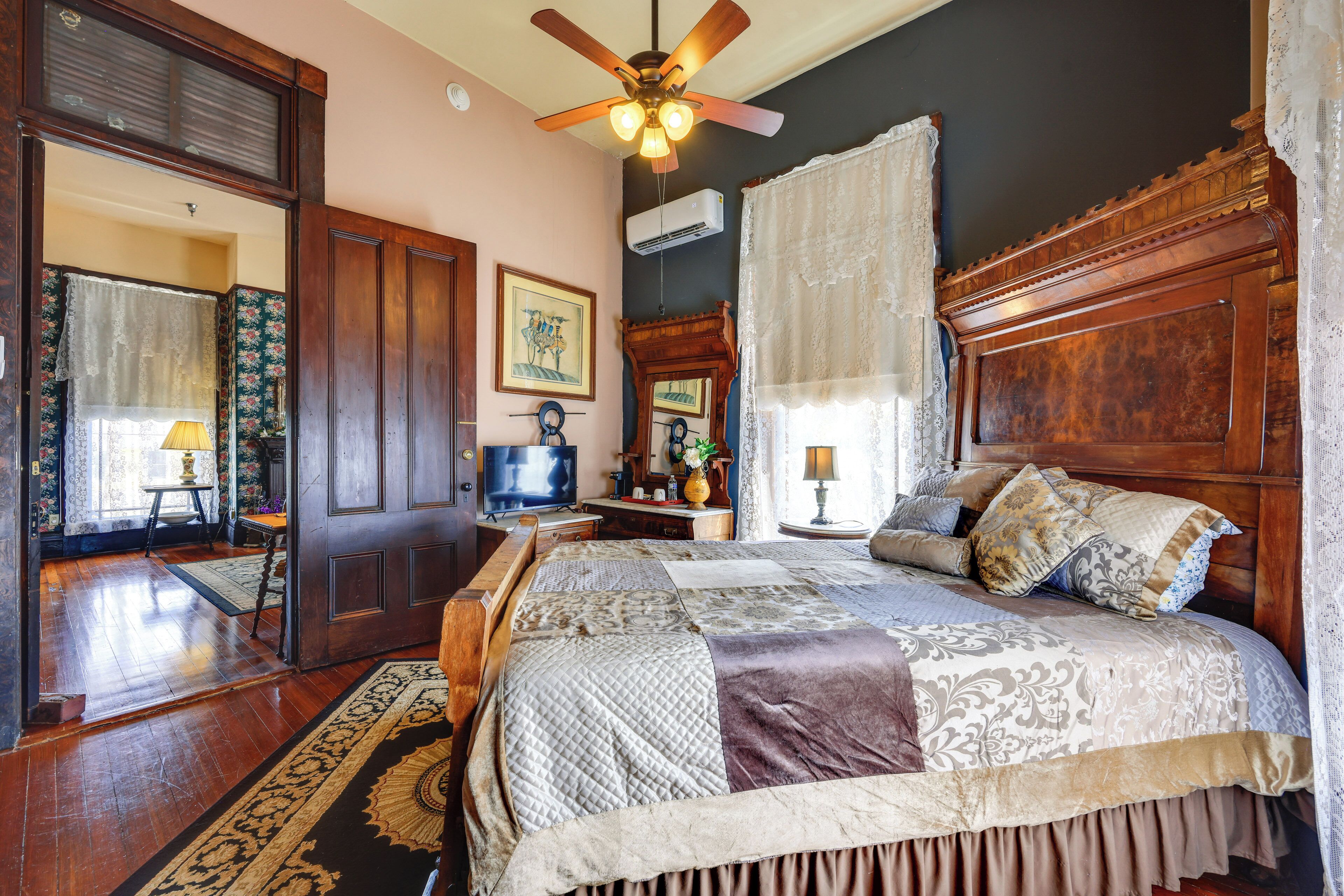 Quarto com cama de madeira, ventilador de teto, televisão e janela com cortinas.