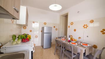 Uma cozinha moderna com área de refeições, equipada com geladeira, pia e mesa posta para dois, incluindo pratos, talheres e uma tigela com frutas.
