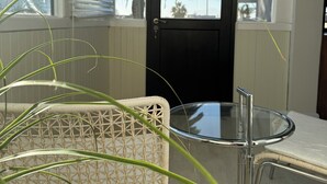 Quarto com cadeira de vime, mesa de vidro e porta que dá para o exterior.